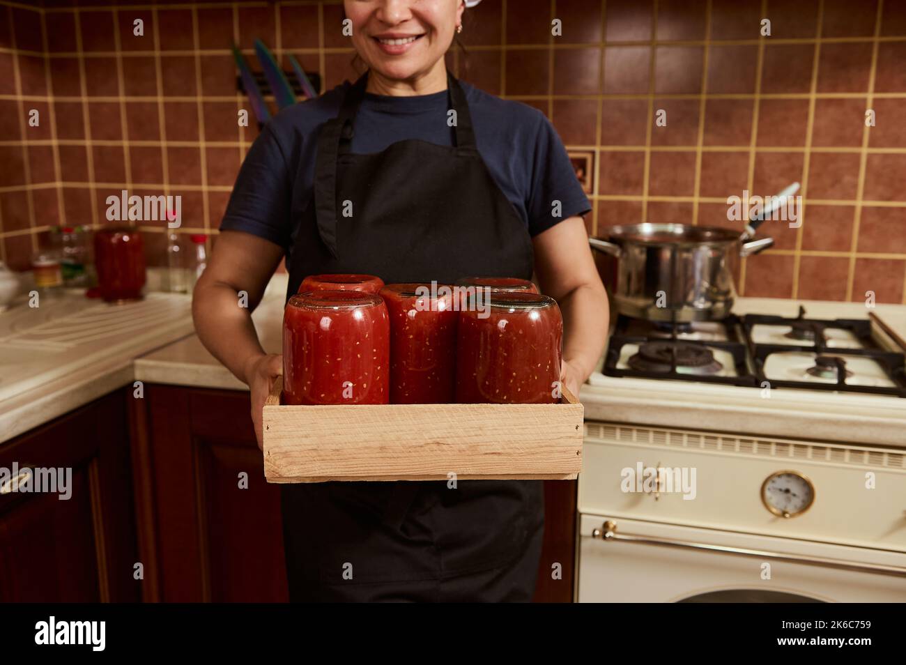 Pleasant woman housewife in black chef's apron holding a wooden crate ...