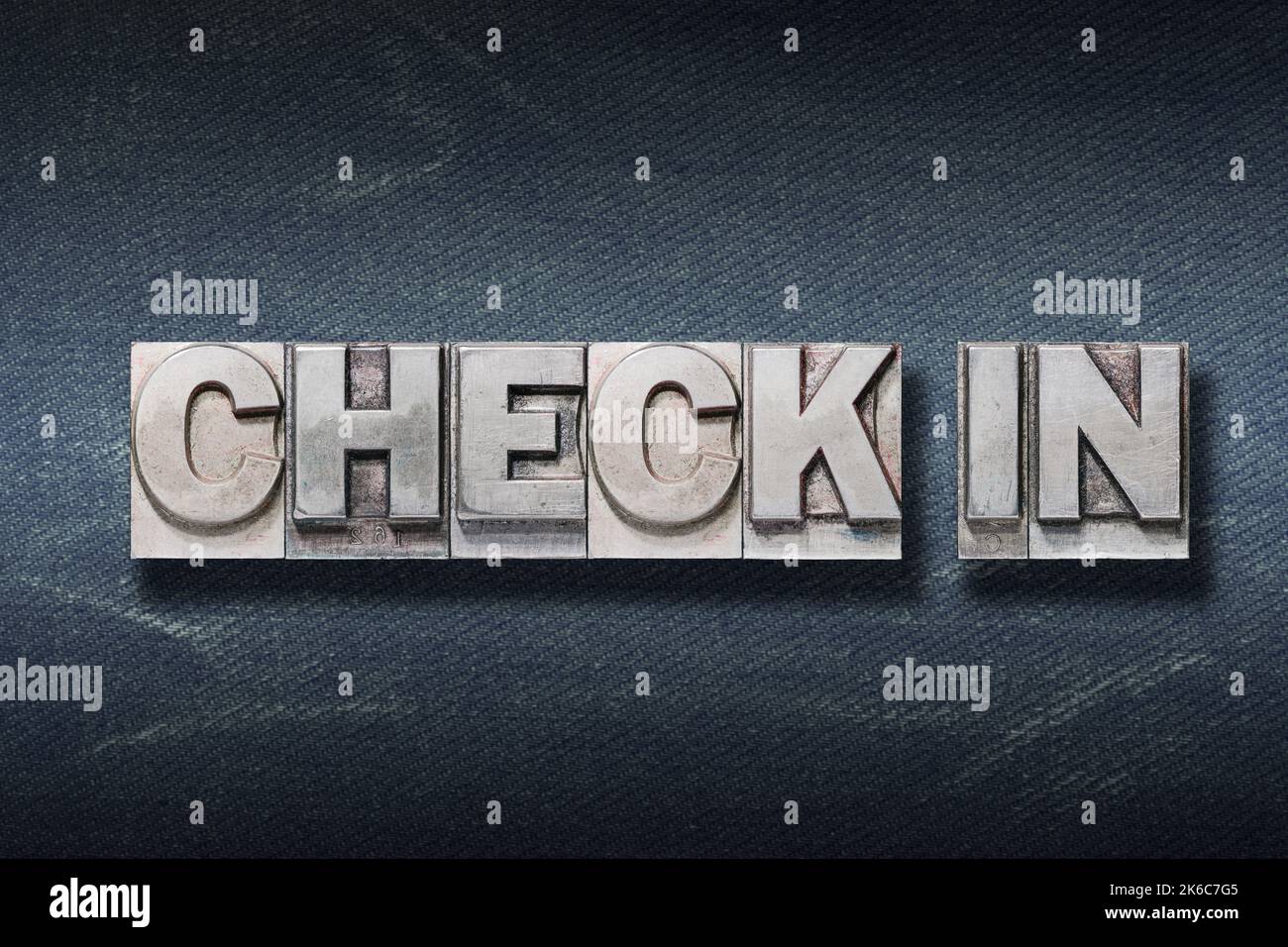 check in phrase made from metallic letterpress on dark jeans background ...