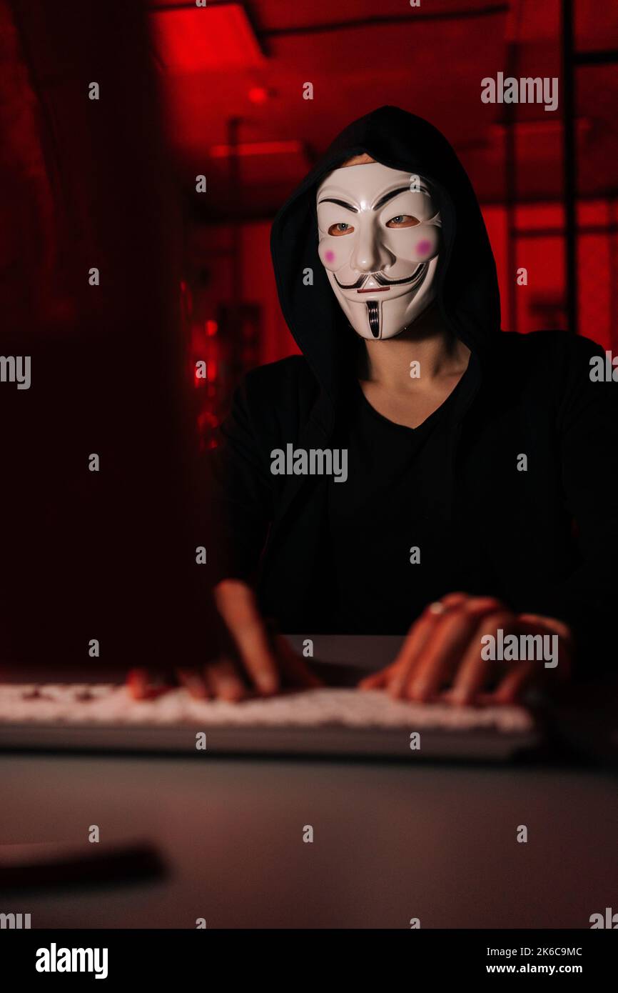 Close-up vertical shot of wanted hacker man wearing anonymous mask and sweatshirt with hood ...