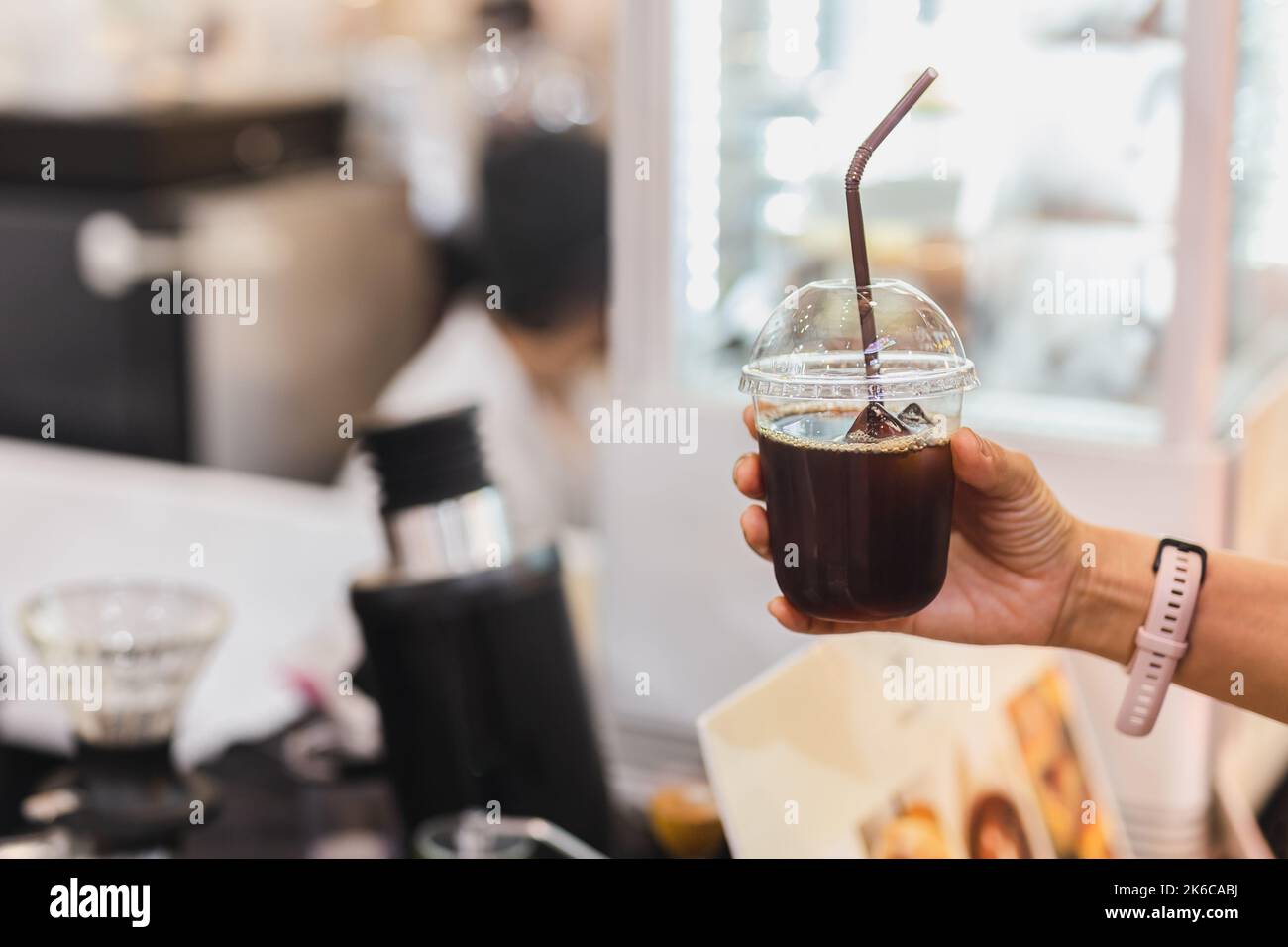 Woman customer hand holding ice coffee in plastic glass with straw ...