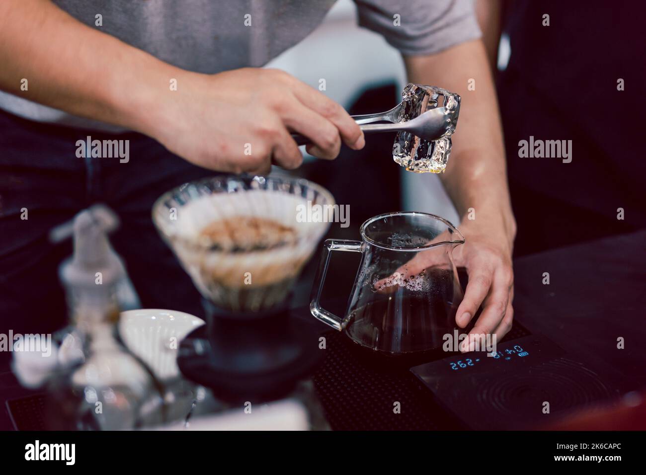 Barista making iced coffee by putting an ice into a glass jar with ...