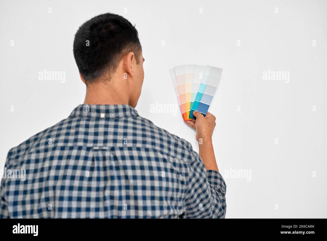An Asian man holds up pastel swatches against wall looking to decide on ...