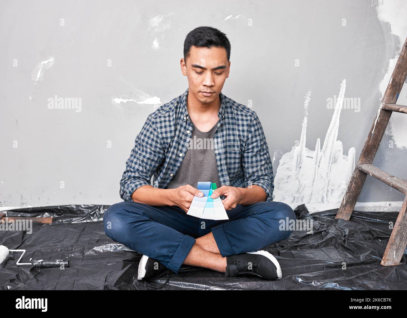 A young Asian man sits on the floor choosing paint colour from swatches ...