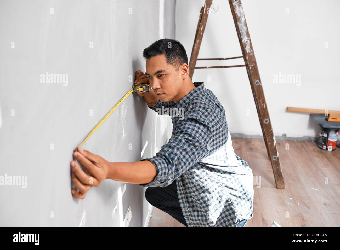 An Asian man measures against the wall using measuring tape doing home ...