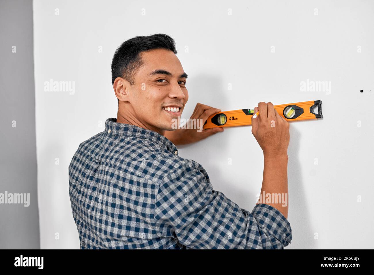 An Asian man smiles while using spirit level against wall doing home ...