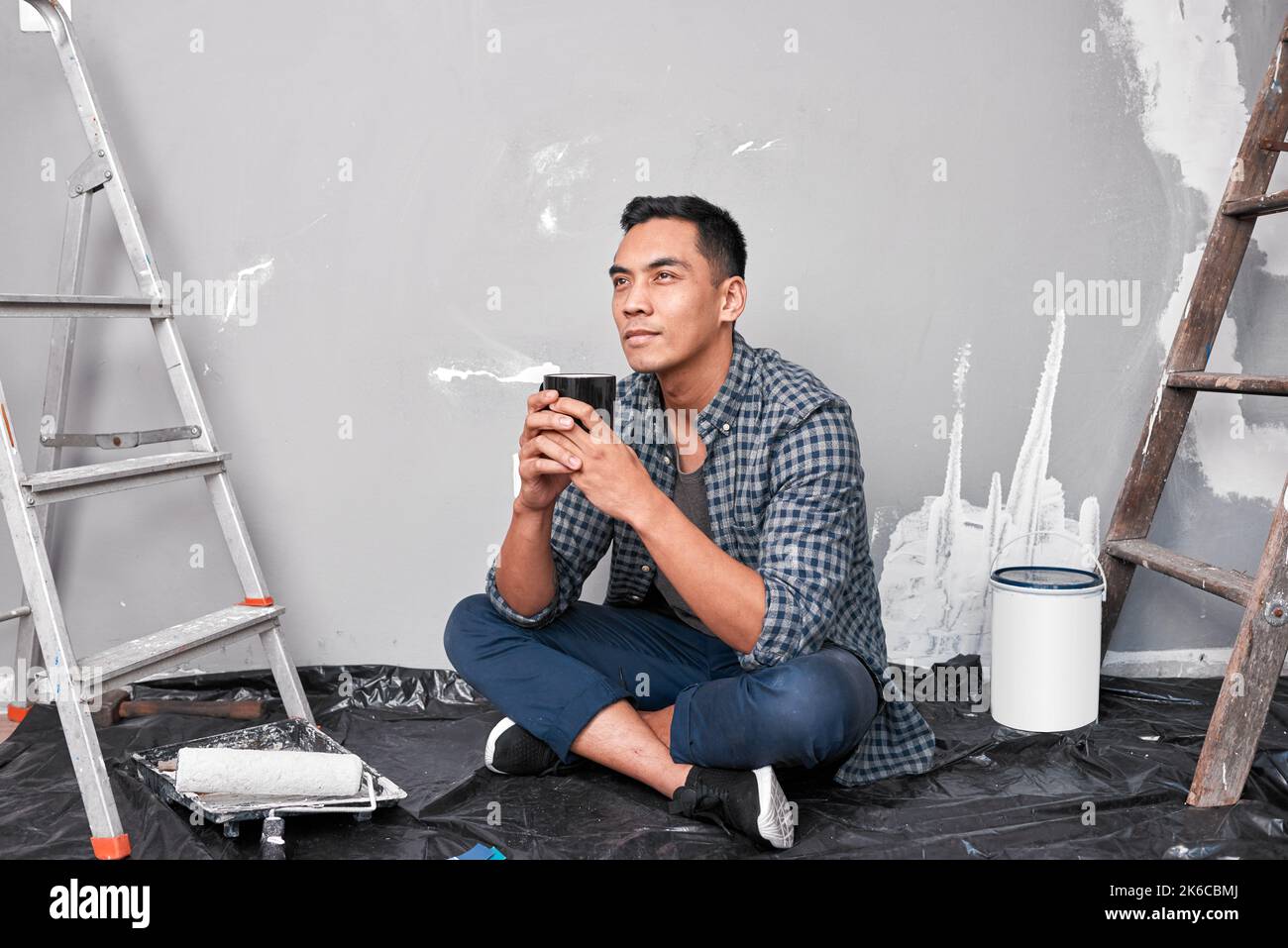 An attractive young Asian man sits on the floor taking a coffee break ...