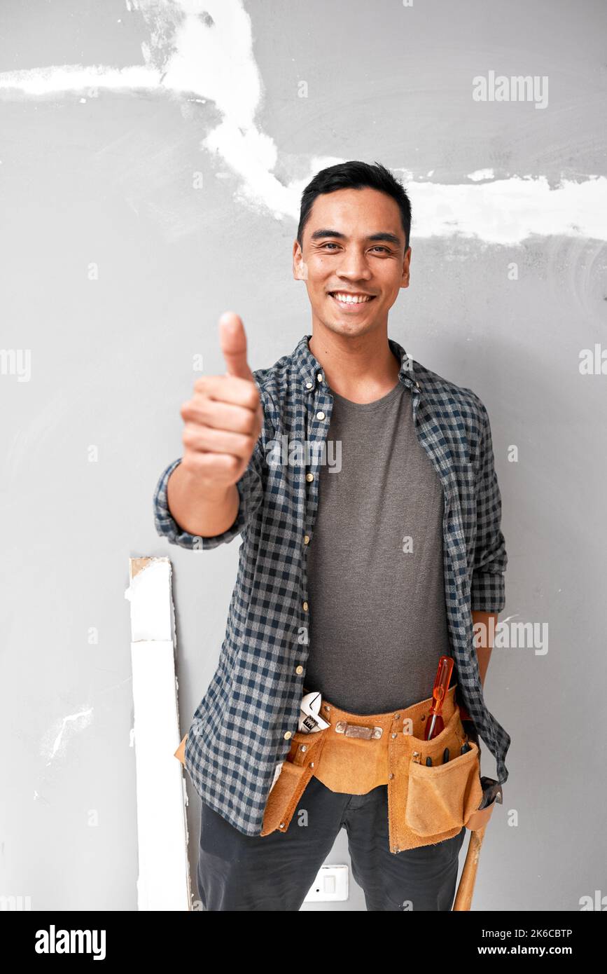 An attractive young Asian man gives thumbs up while doing home DIY ...