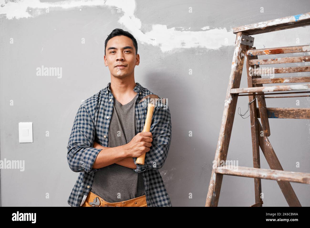 A confident Asian man holds hammer with arms crossed ready for home DIY ...