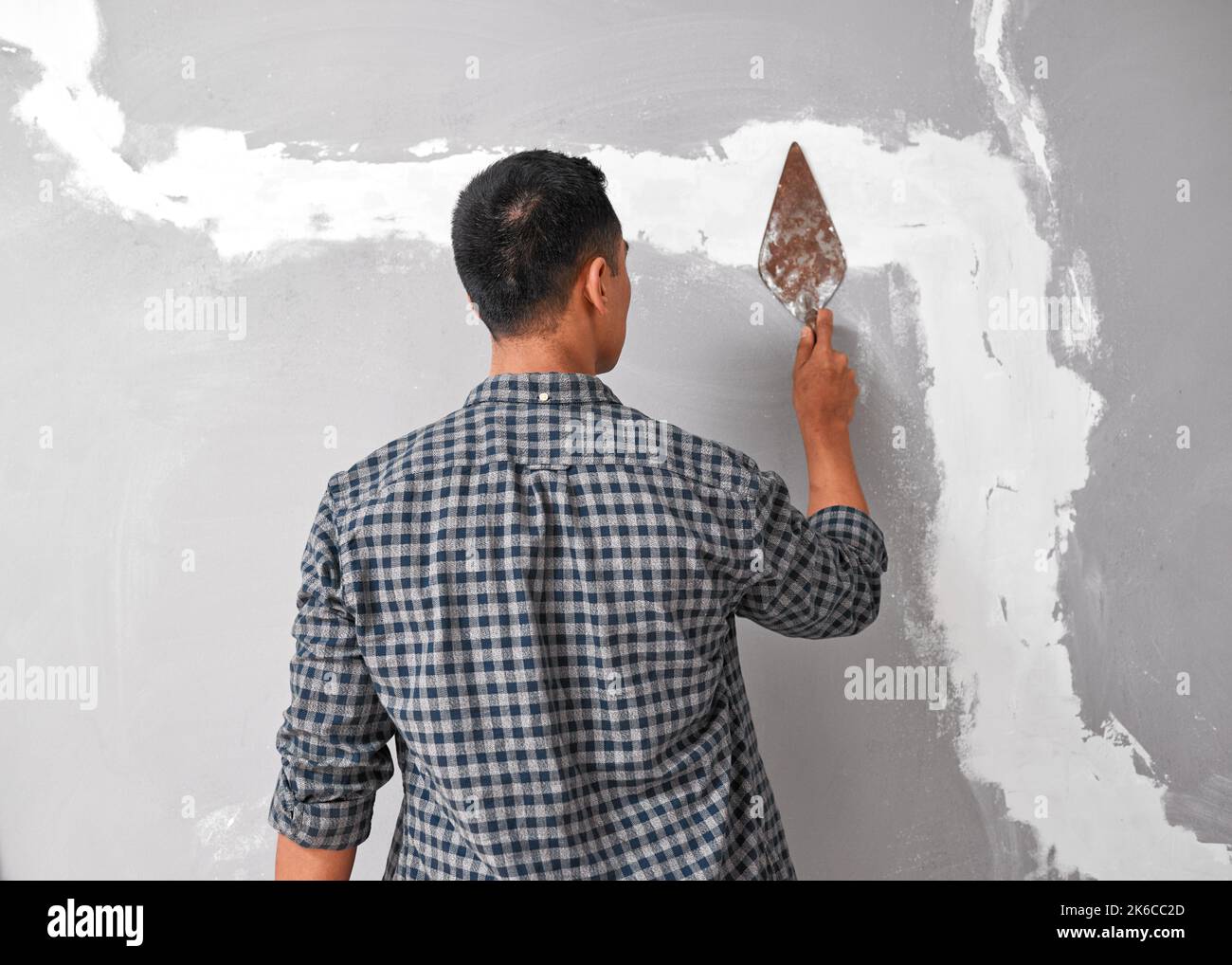 An Asian man smooths plaster over cracks in wall with a trowel home fix ...