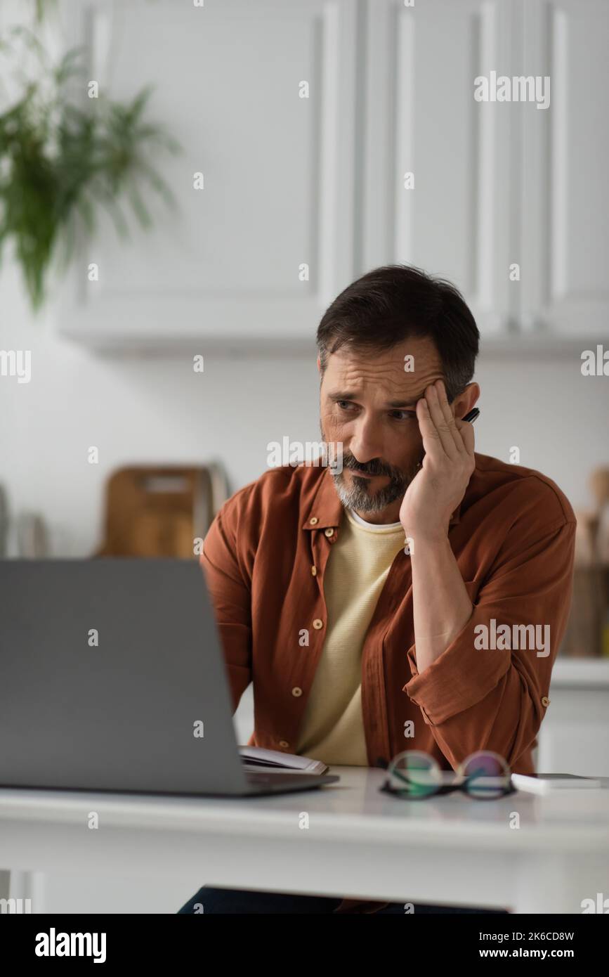 tired man looking at blurred laptop in kitchen and suffering from ...