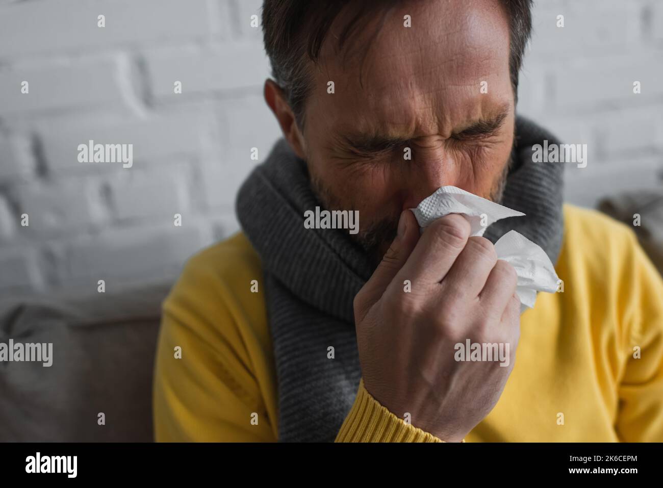 sick man in warm scarf holding paper napkin and sneezing with closed ...