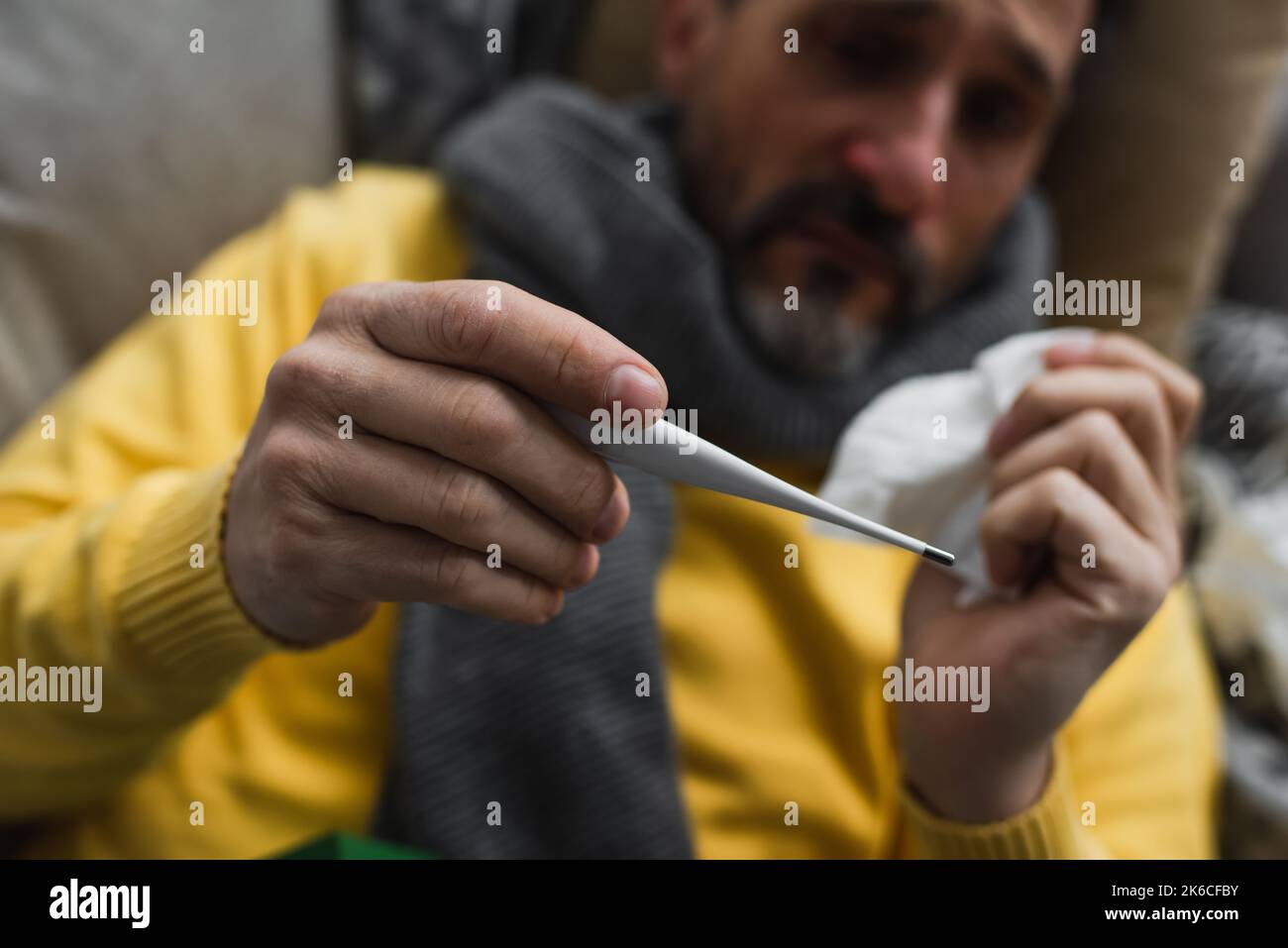 selective focus of electronic thermometer in hand on sick man suffering ...