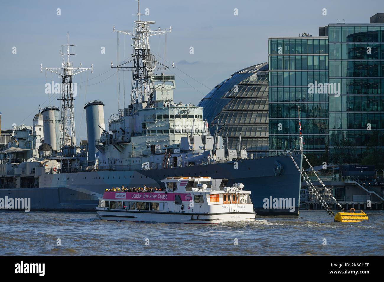 London Eye river cruise boat passes HMS Belfast moored against the ...