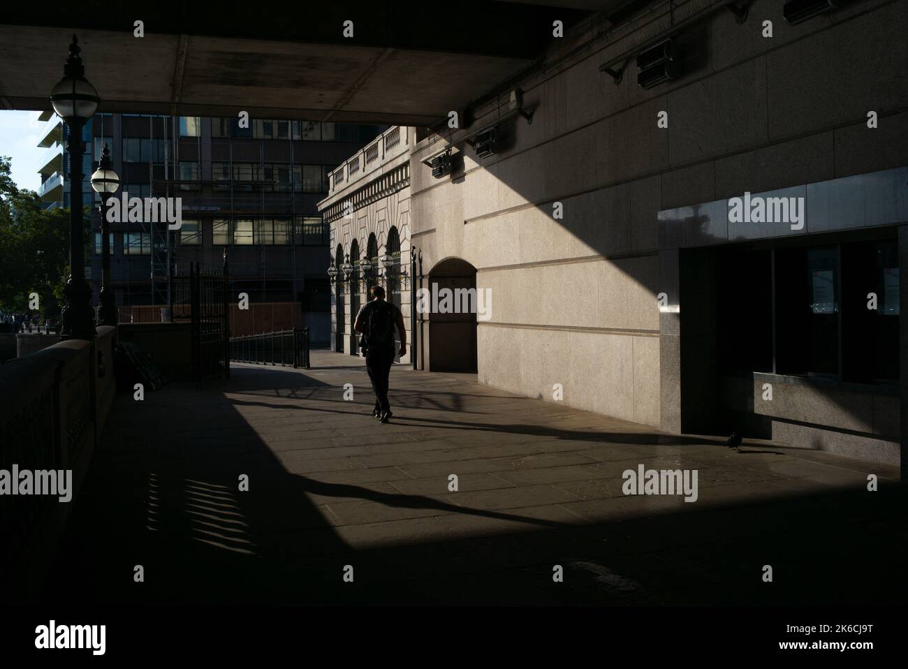 A man walks in silhouette at London Bridge wharf under the London ...