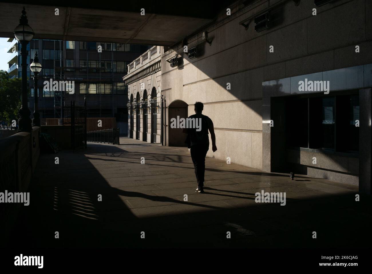 A man walks in silhouette at London Bridge wharf under the London ...