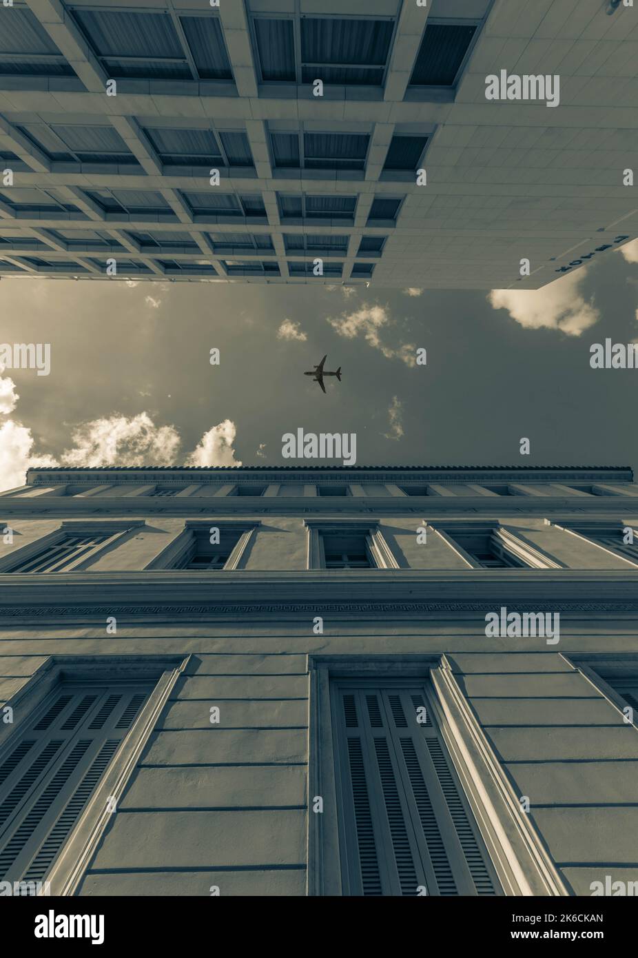 A vertical low-angle shot from in between buildings of an airplane in ...