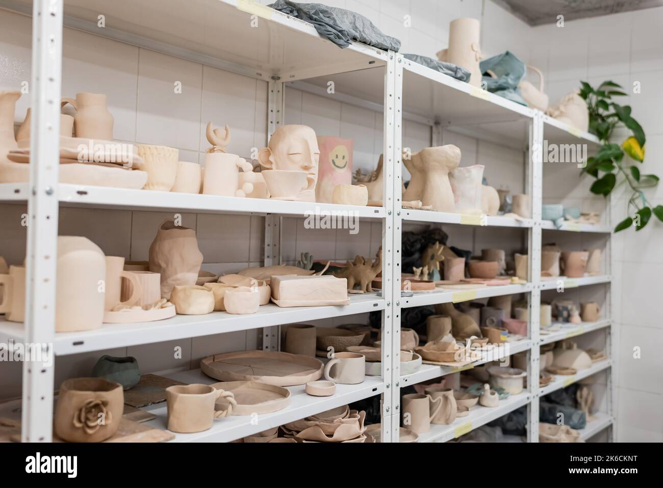 different clay sculptures near cups and bowls on shelves of pottery ...