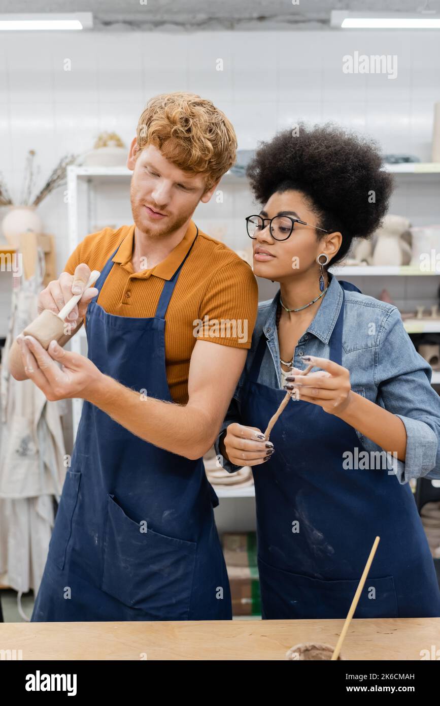 Craftsman holding tool and clay near african american woman in pottery ...