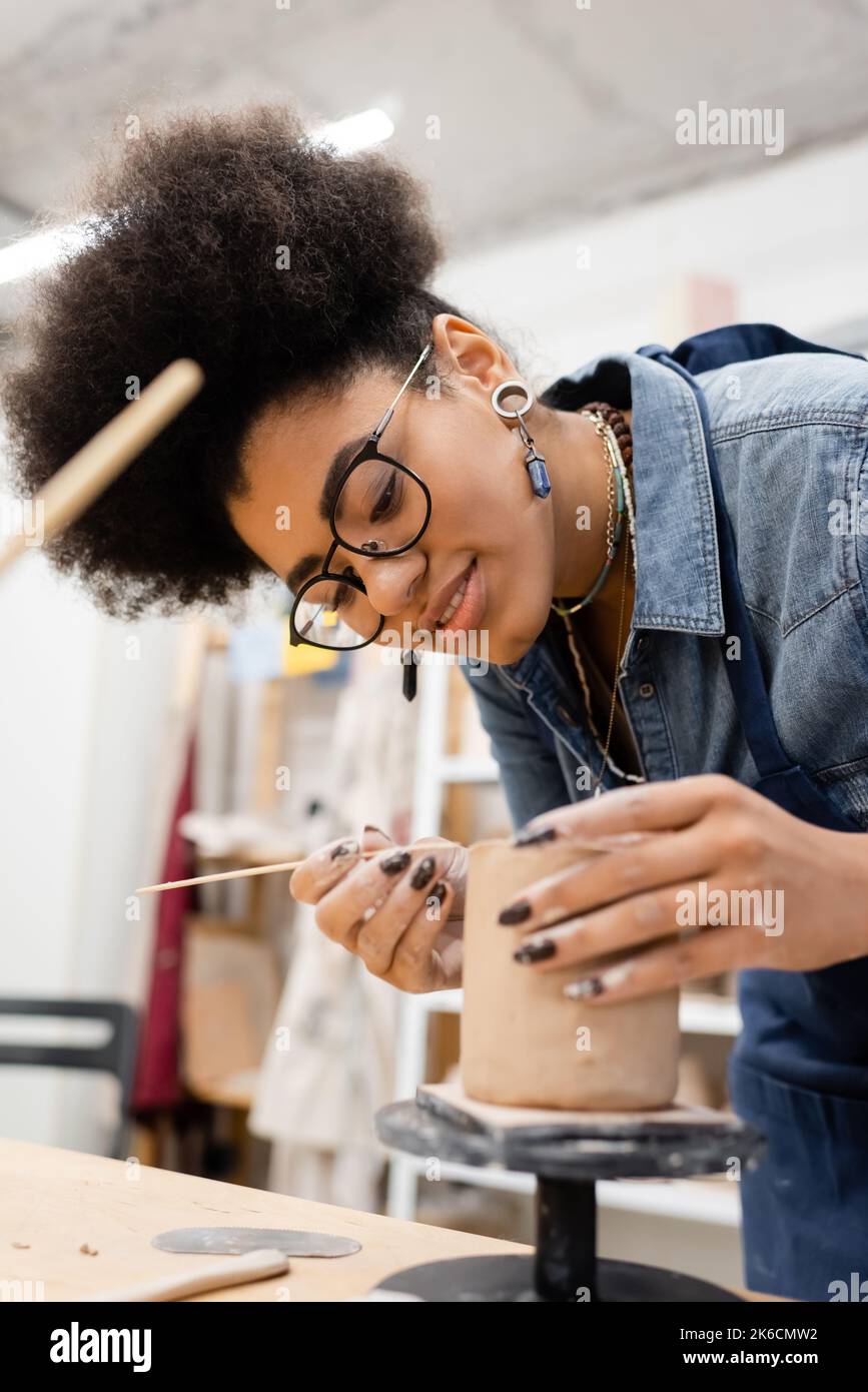 Smiling african american craftswoman making clay sculpture in pottery ...