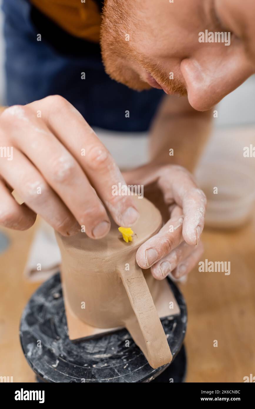 Close up view of bearded artisan pressing tool in clay product in ...