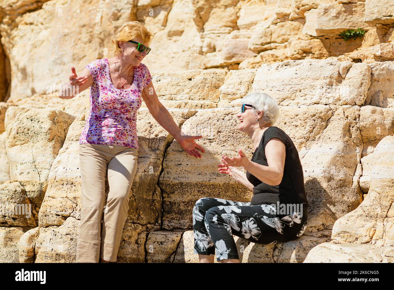 Two elderly women are happy to meet each other, sitting on rock Stock ...