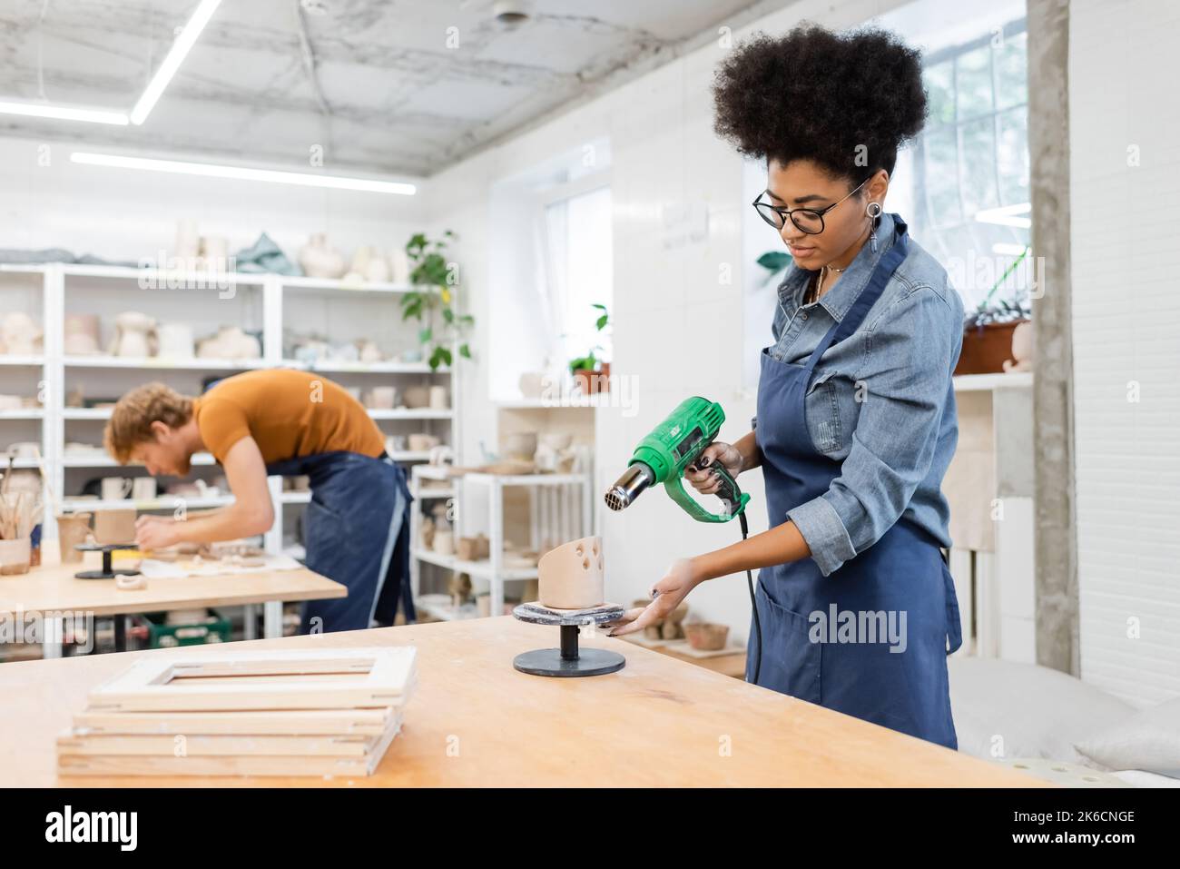 African american woman holding heat gun near clay product and blurred ...