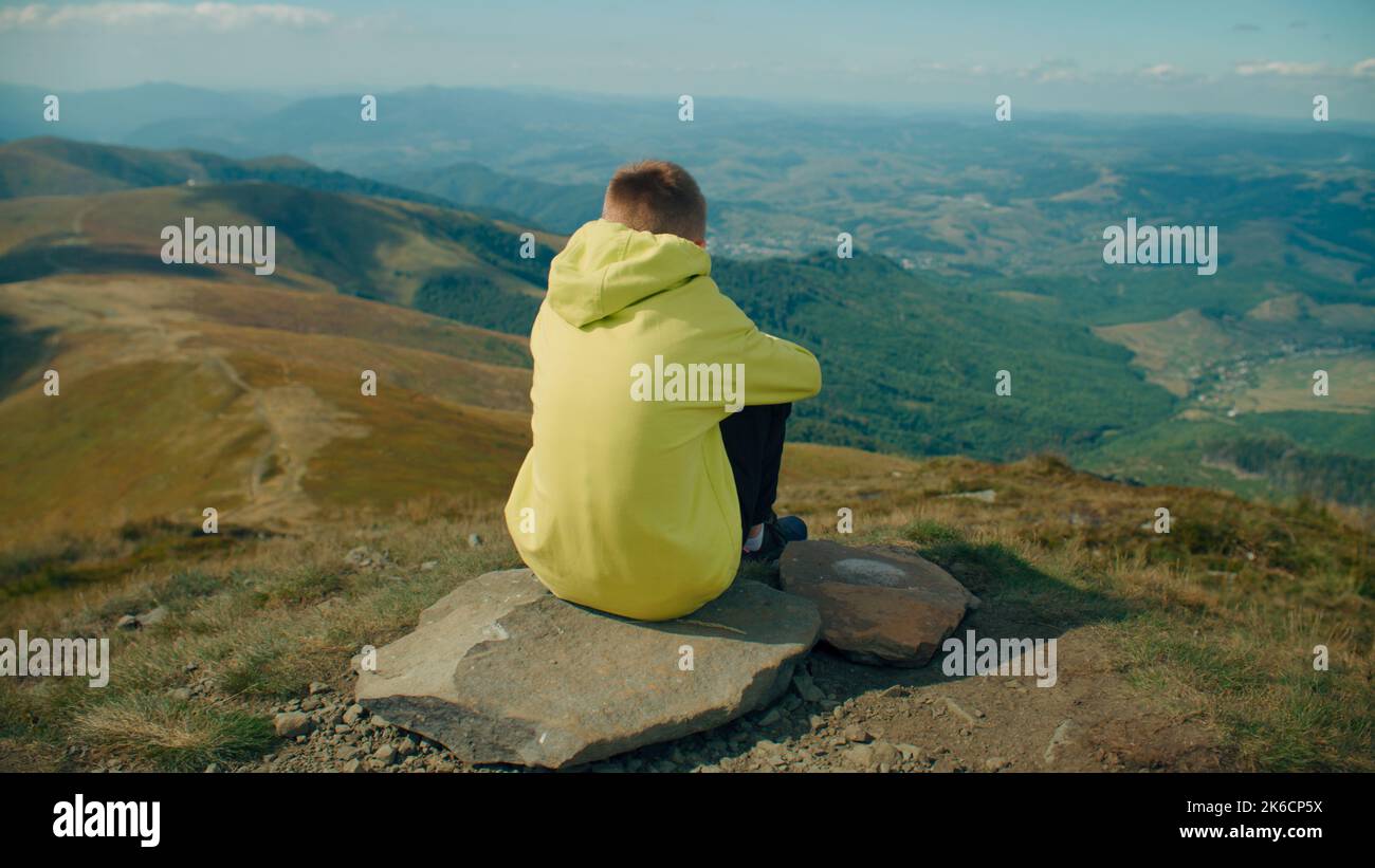 Young guy sitting on stone, watching on beautiful landscape, feeling ...