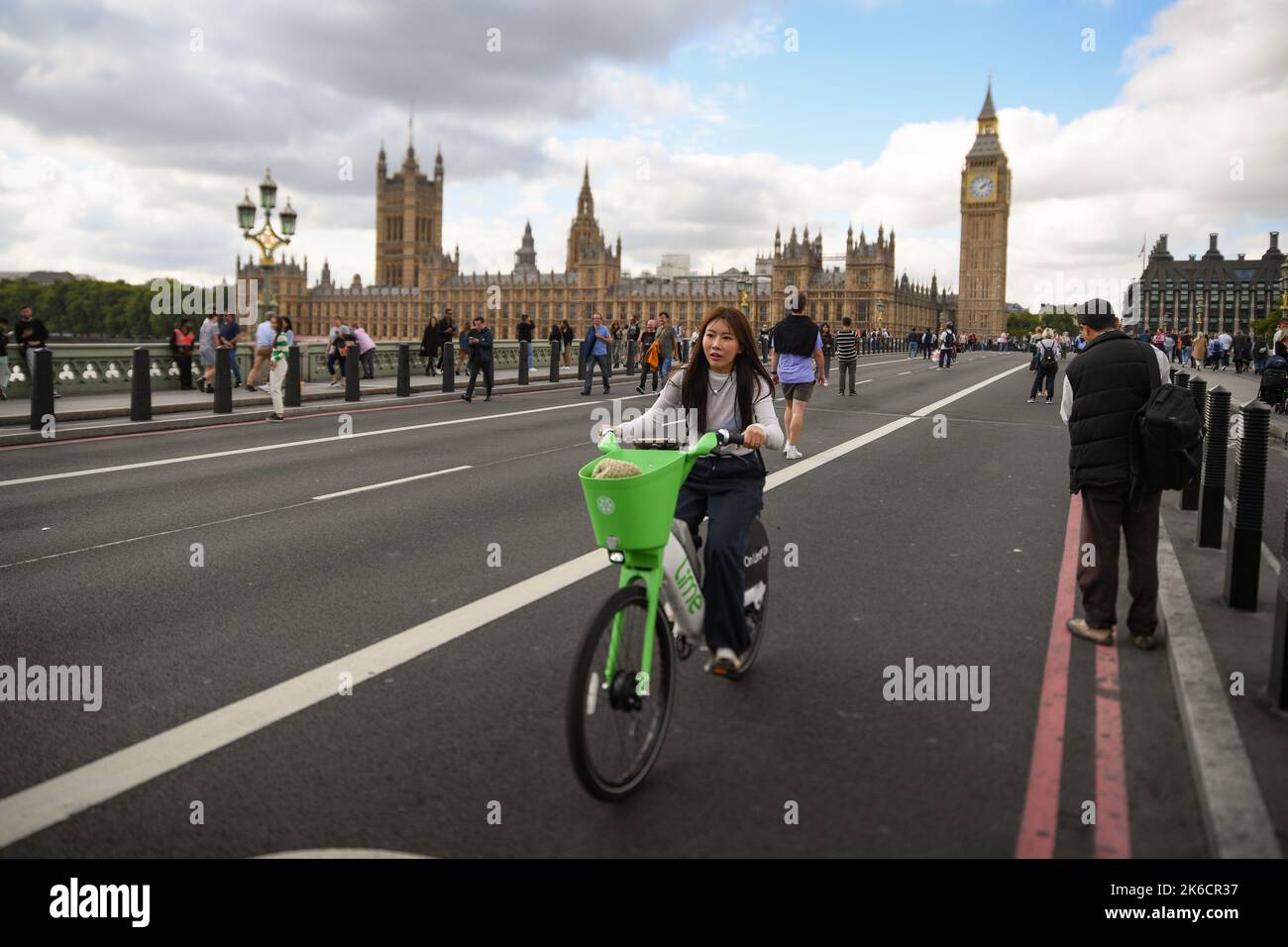 A young Asian women rides a Lime electric bike over Westminster Bridge ...