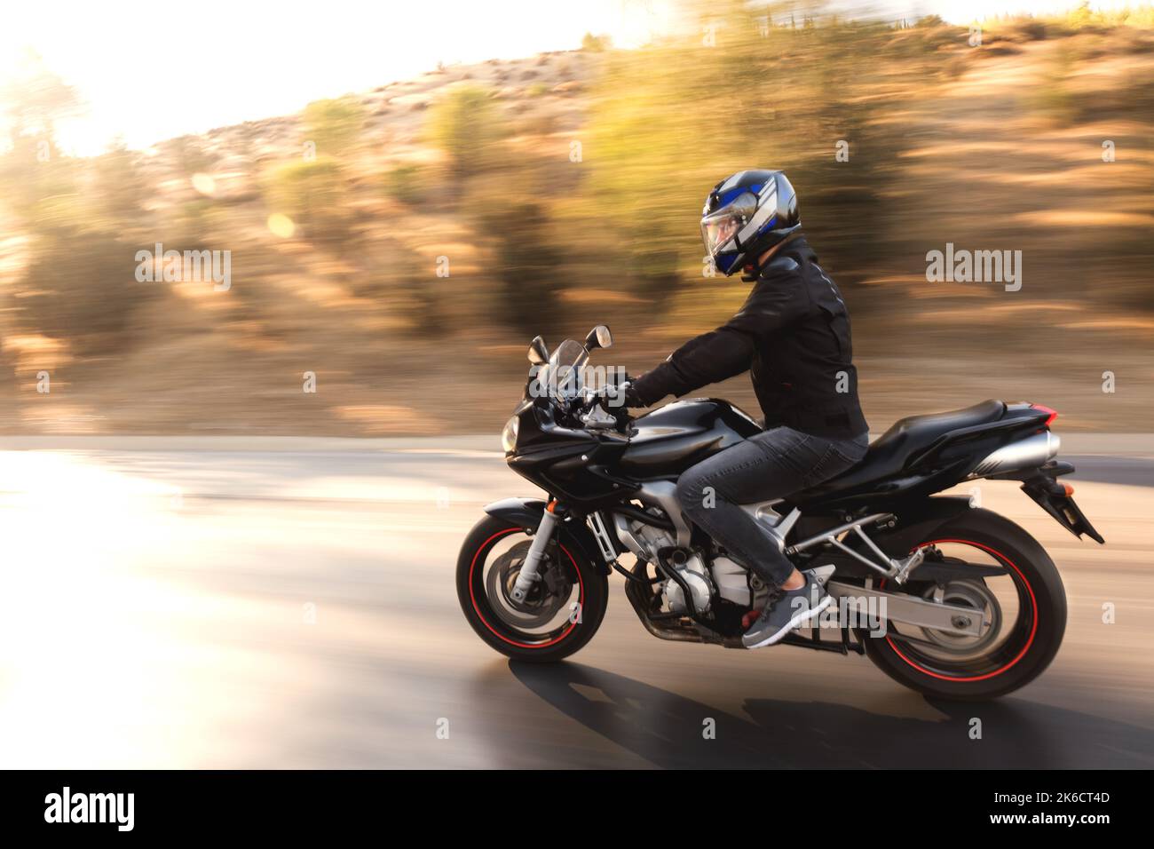 Side view of a biker riding black race motorcycle on the highway with ...