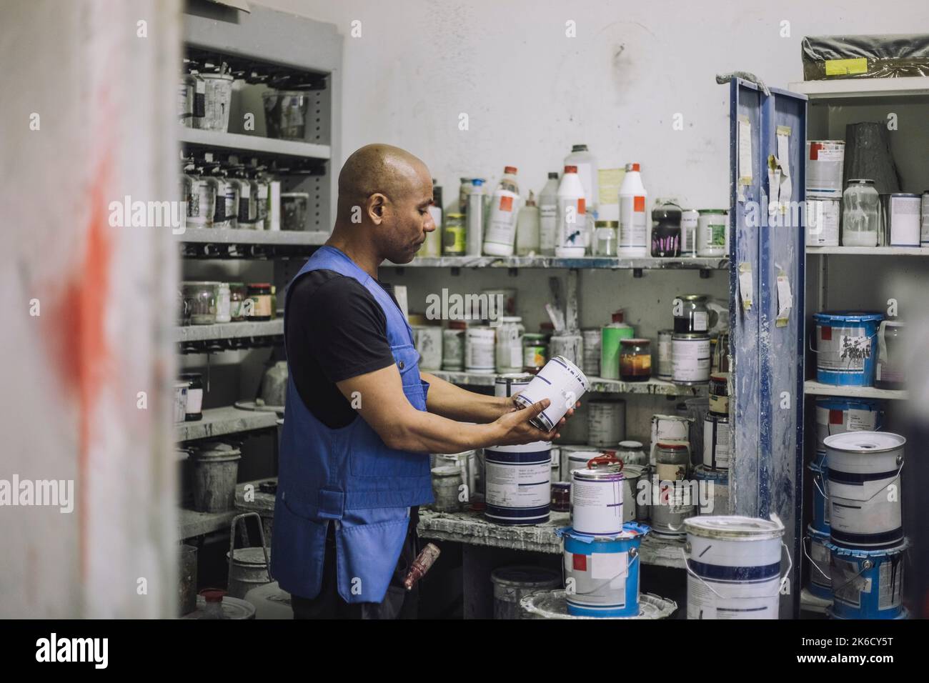 Side view of bald painter examining paint can while working in workshop ...
