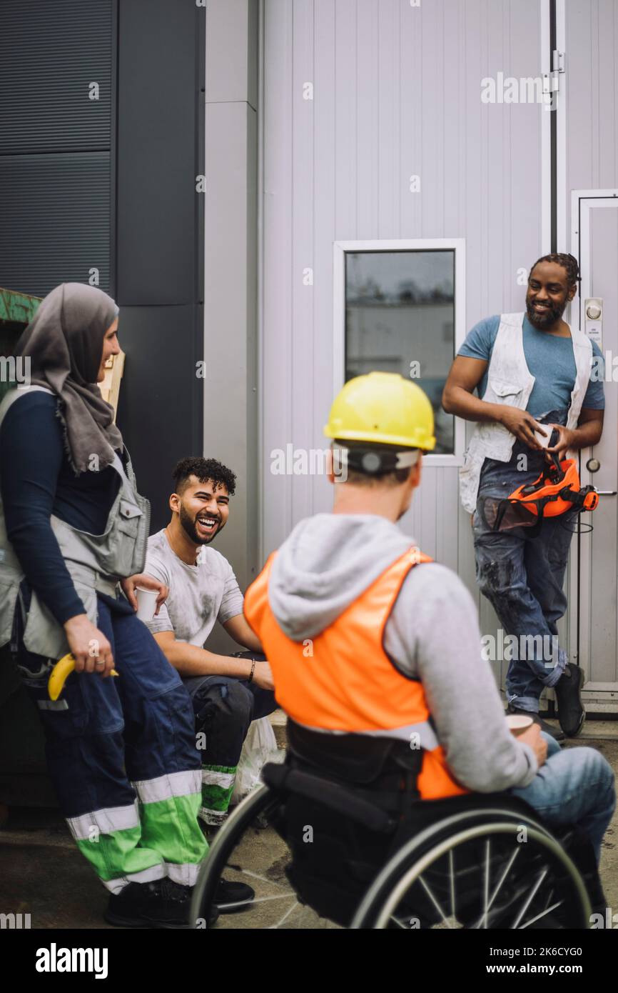 Happy young construction worker talking with male and female colleagues ...