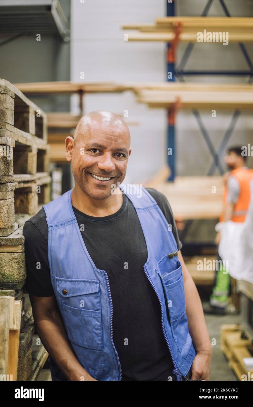 Happy bald carpenter leaning on wooden rack at warehouse Stock Photo ...