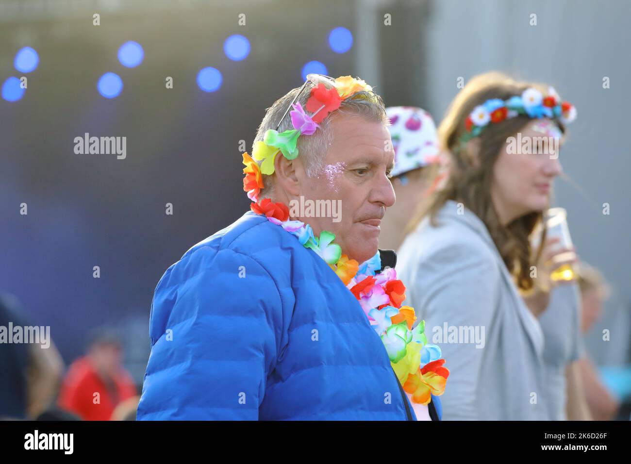 an older man with some face glitter and a colourful Hawaiian lei around ...