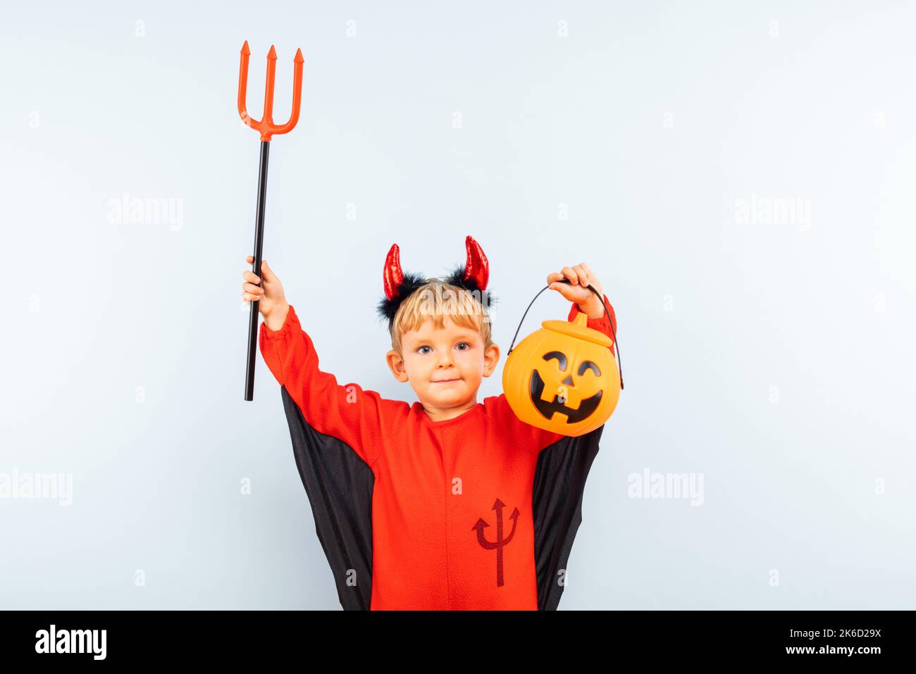 Cute boy in devil halloween costume with trident and pumpkin basket ...