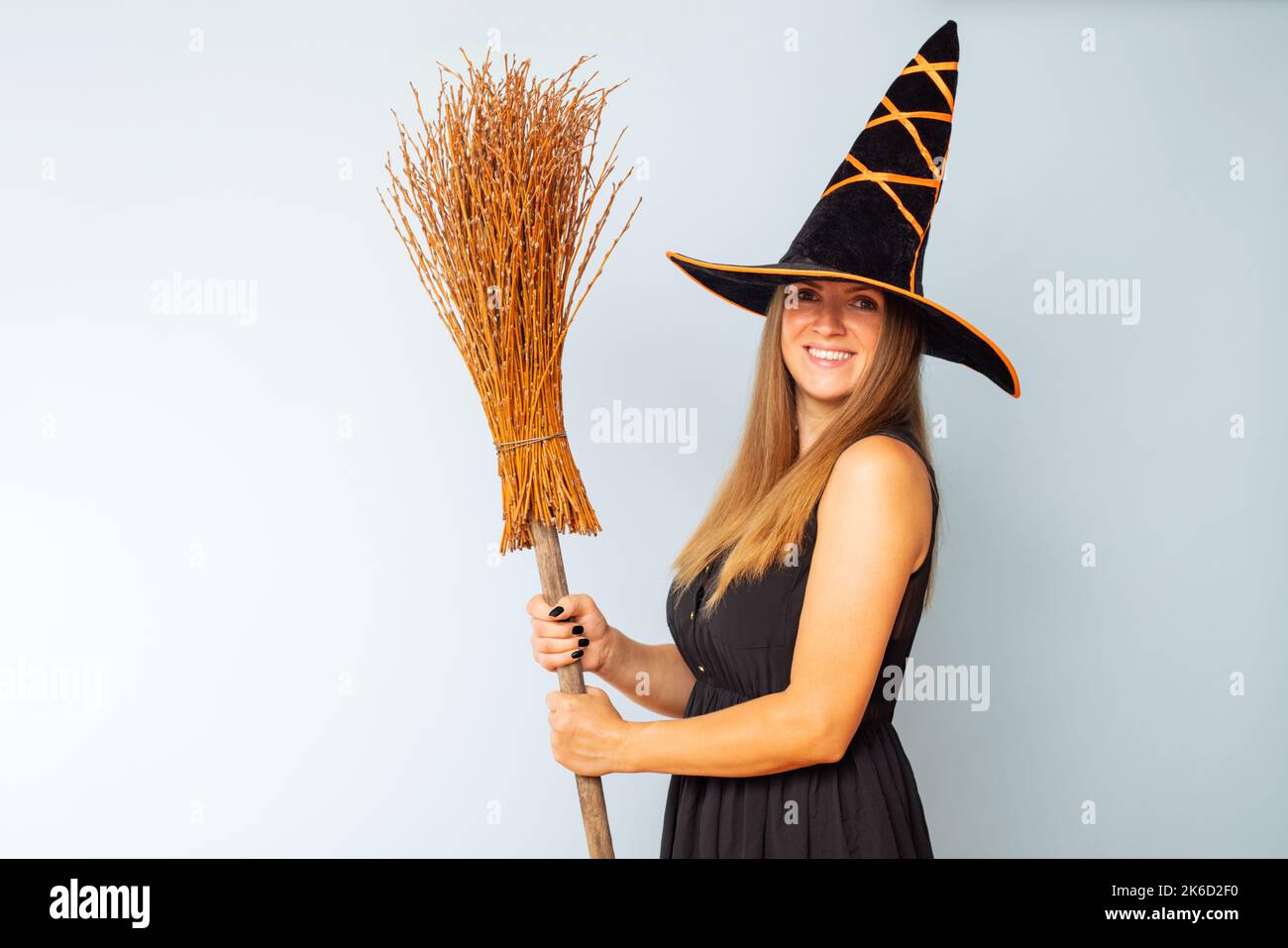 Happy woman in halloween witch costume with broom on a light background ...