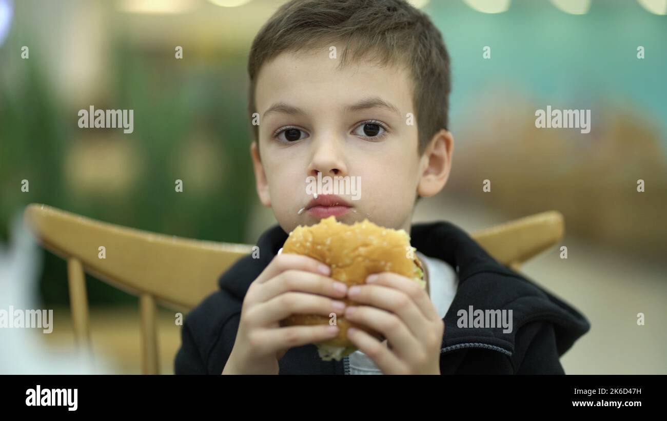 Tired sad boy of seven years old eats a burger at a food court after a ...