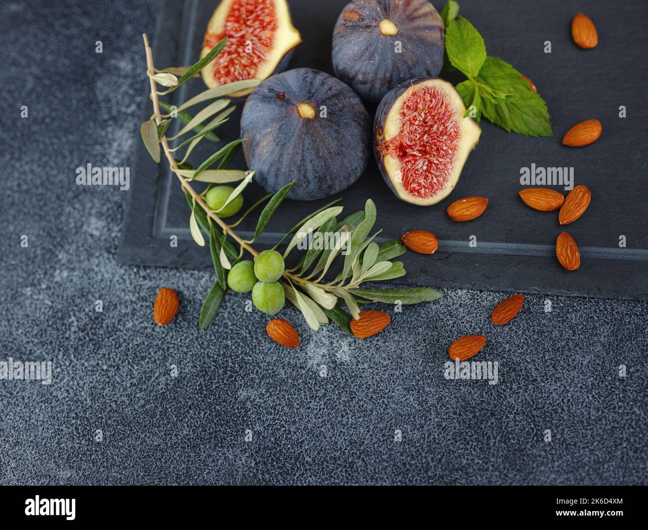 fresh ripe figs fruit almond nuts and olive branch on dark table ...