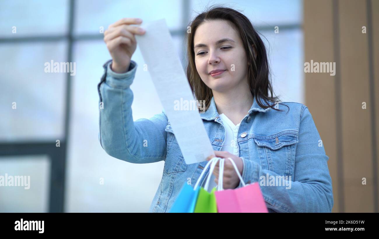 Young woman looks at the prices of goods on a cash receipt after ...