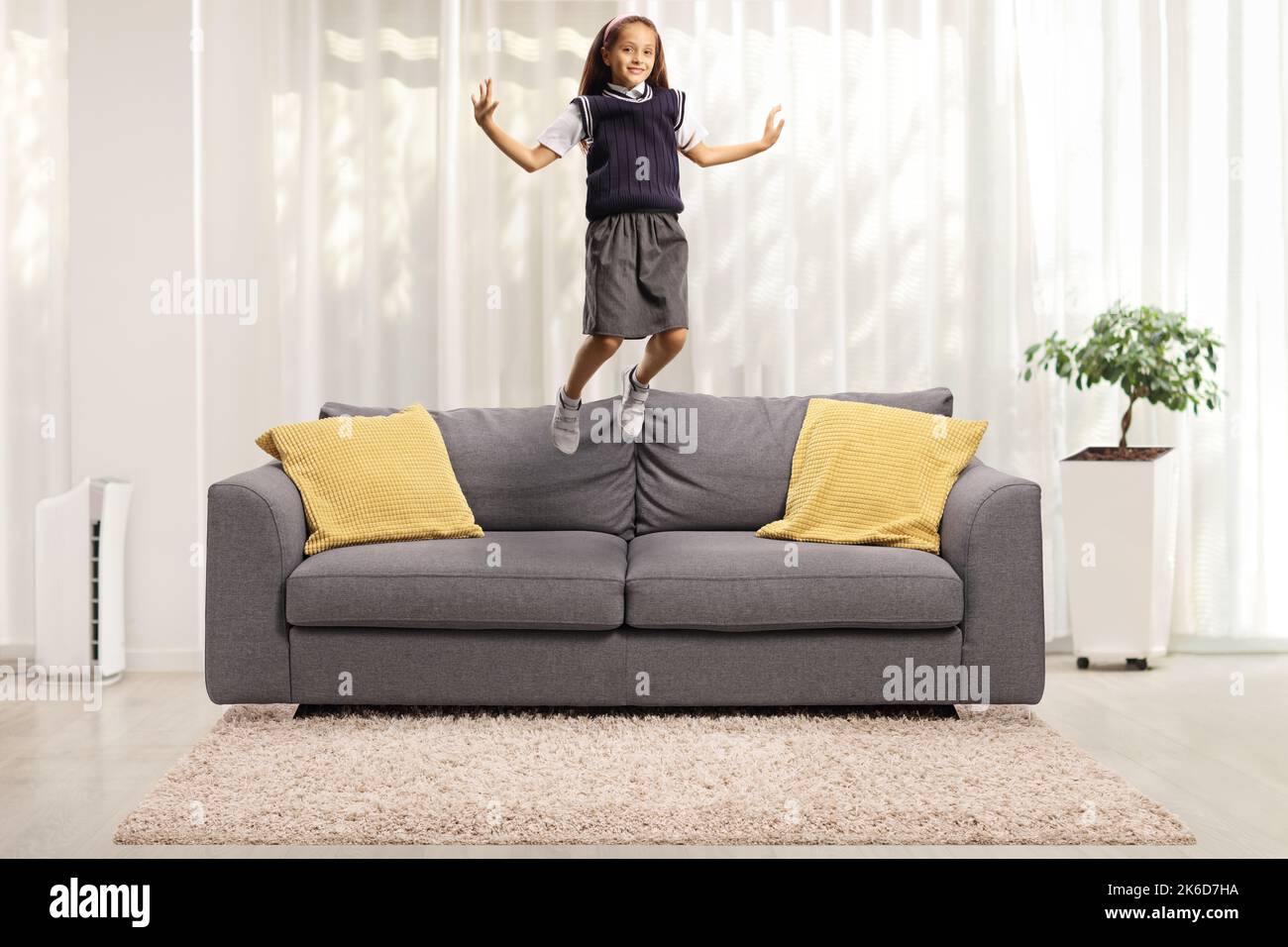 Girl in a school uniform jumping on sofa at home Stock Photo - Alamy