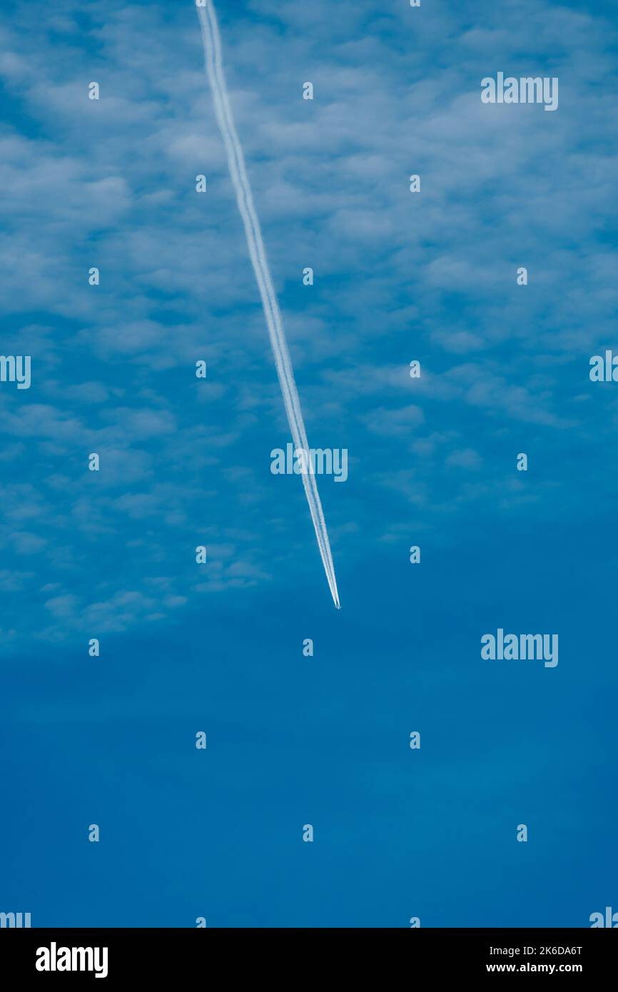 Jet airplane flying in a blue sky with clouds forming long white ...