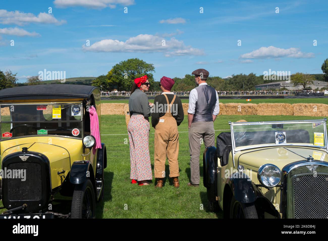 Three people in period dress next to two Austin 7 cars, a display to ...