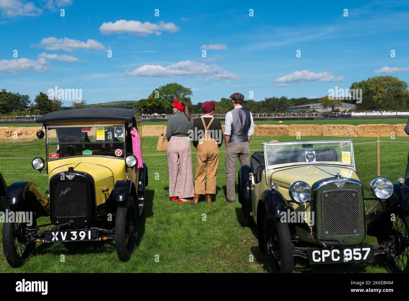 Three people in period dress next to two Austin 7 cars, a display to ...