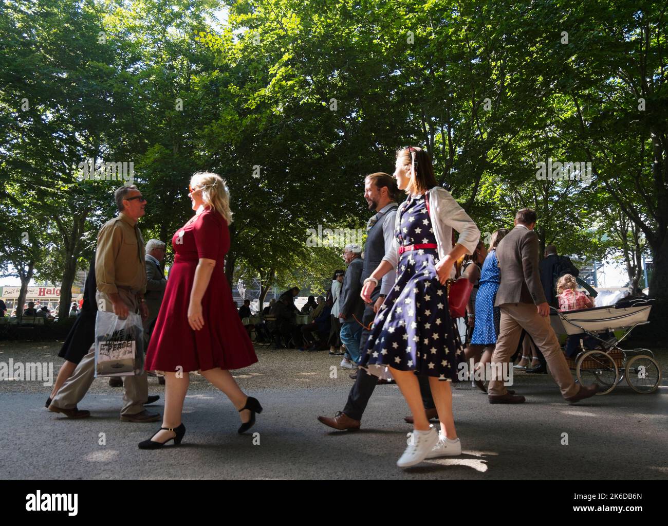 People in vintage period attire walking past tree covered seating area ...