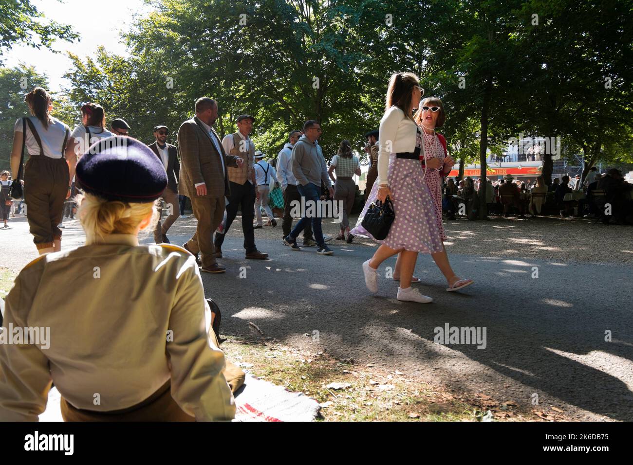 People in vintage attire walking past a woman in ATS uniform sitting on ...