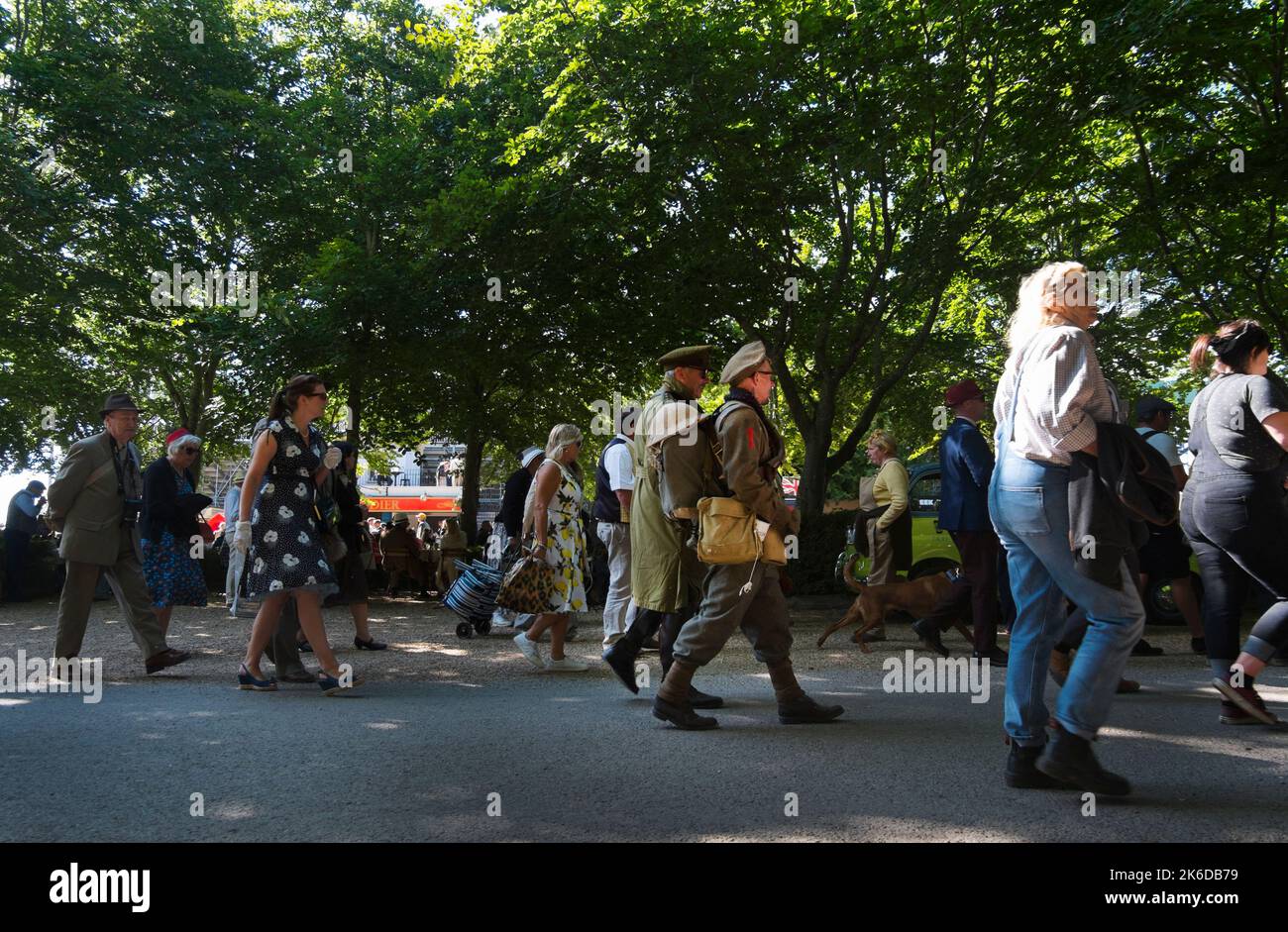 People in vintage period attire walking past tree covered seating area ...