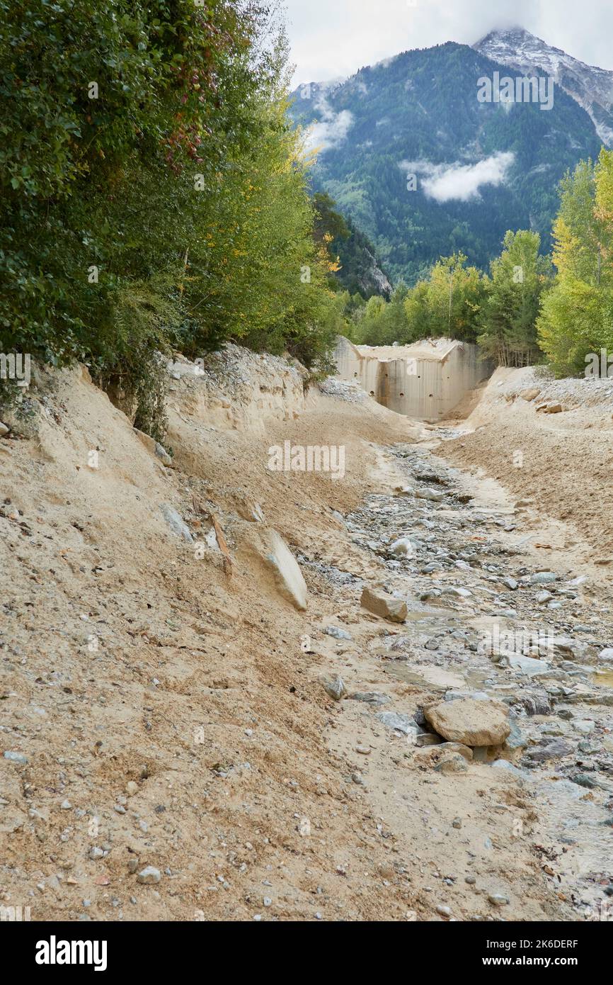 A dry river bed surrounded by trees and a foggy mountain in Leukerbad ...