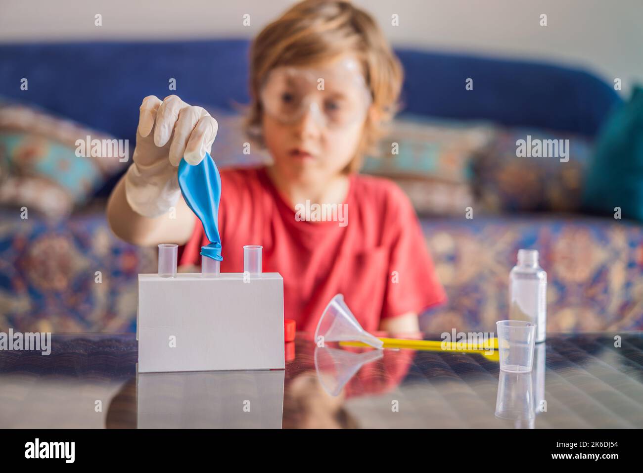 Kid boy doing chemical experiment at home. Child with protective glasses study using pipette ...