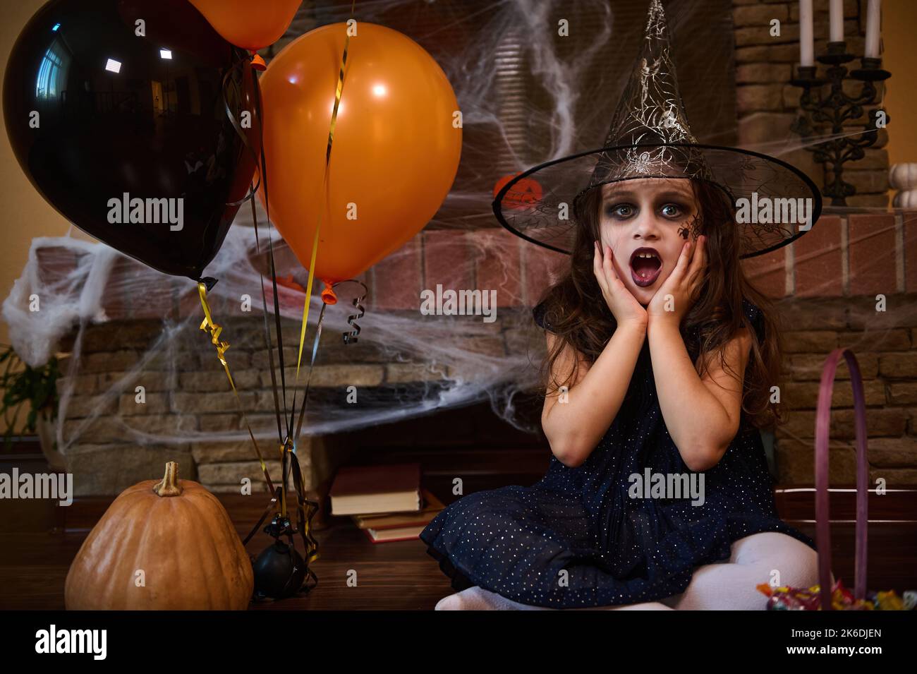 Charming little girl, dressed in witch, sits near orange black balloons ...