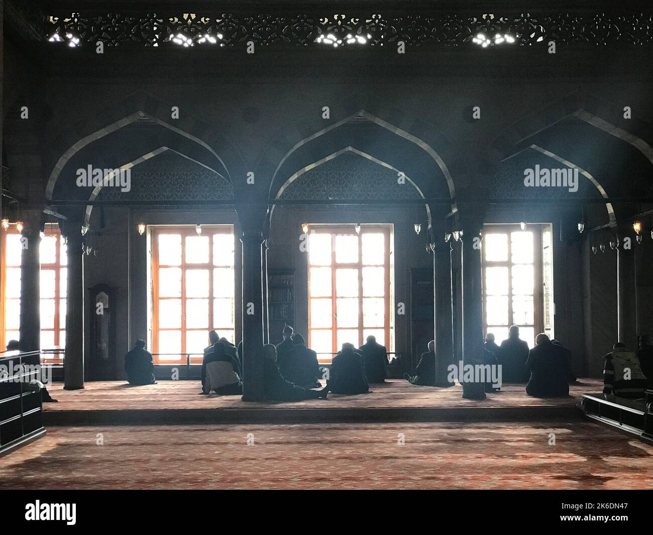 A group of people worshiping in a mosque against windows with sunlight ...