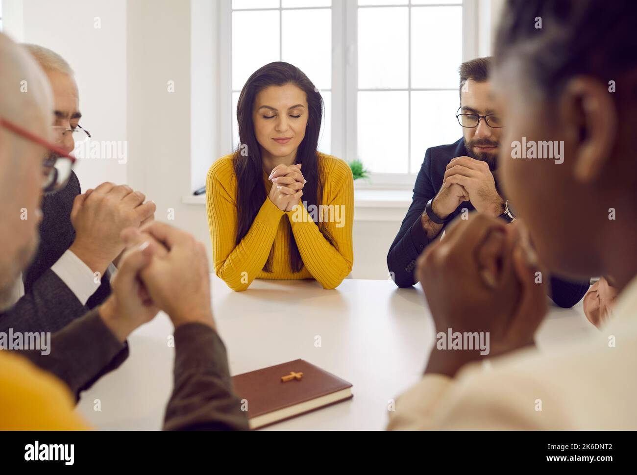 Diverse group of people praying to Lord sitting together around table ...